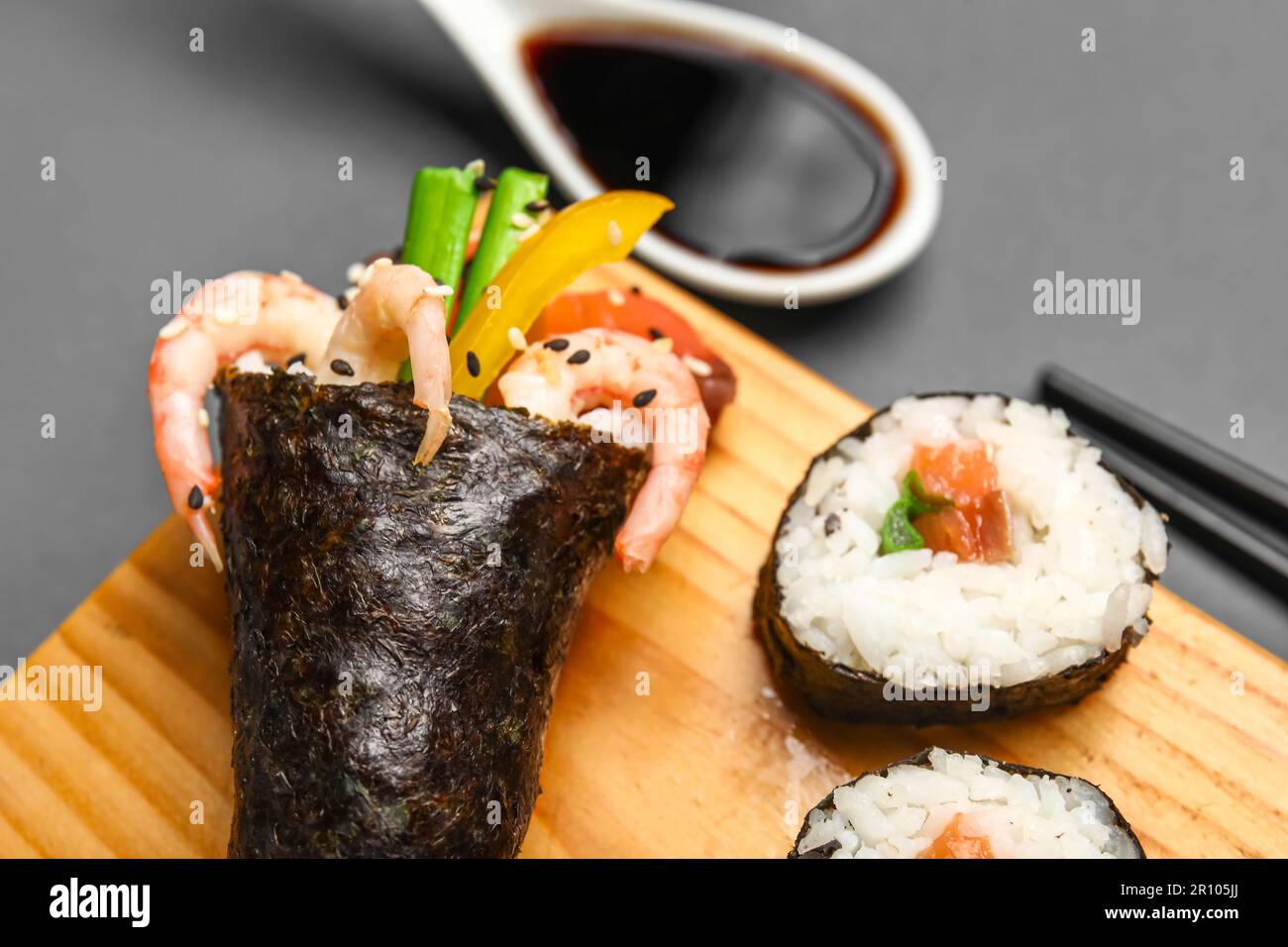 Wooden board with tasty sushi cone, rolls and soy sauce on dark ...