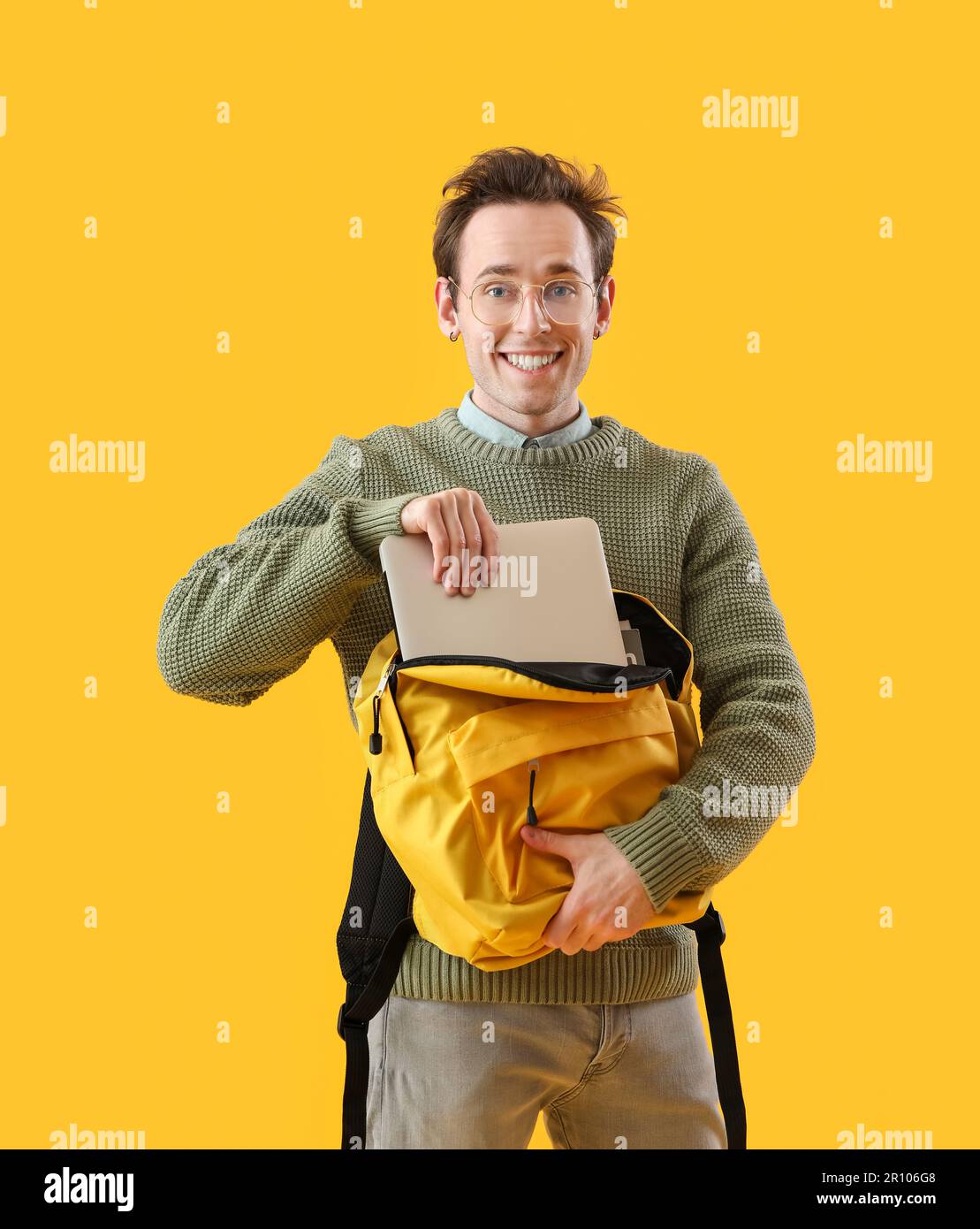 Male student putting laptop in backpack on yellow background Stock ...