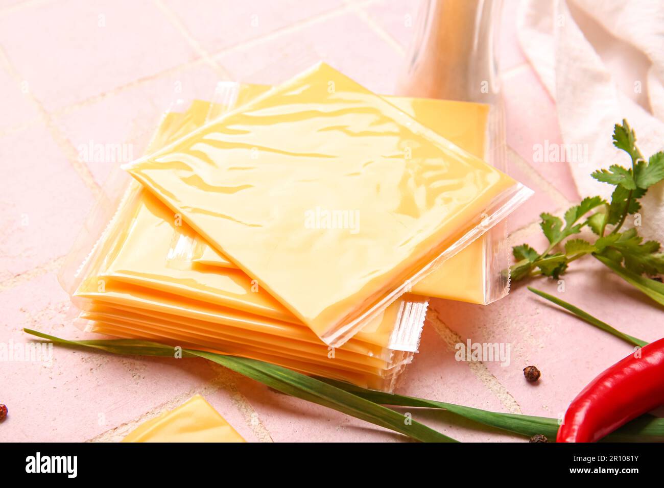 Slices of tasty processed cheese with scallions and chilli on pink tile ...