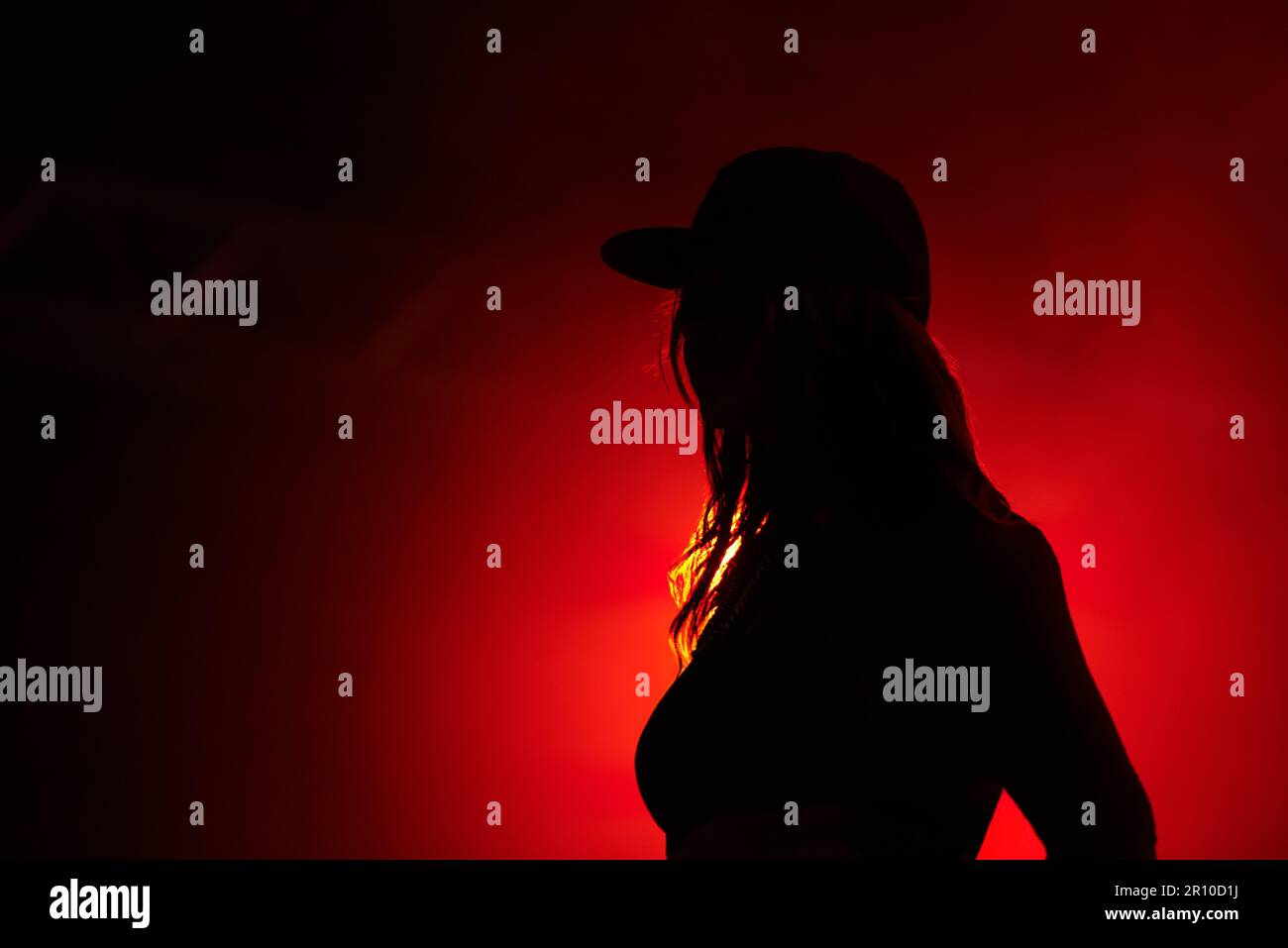 Trendy partygoer in silhouette. A young woman wearing a cap backlit by ...