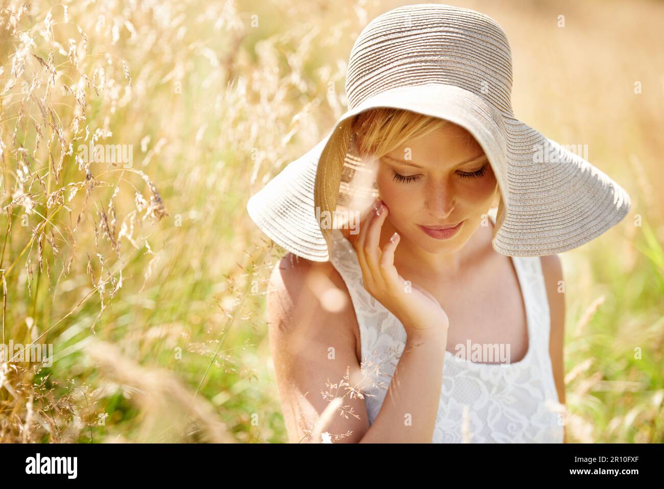 Protecting her skin from the sun. Beautiful young woman wearing a straw ...
