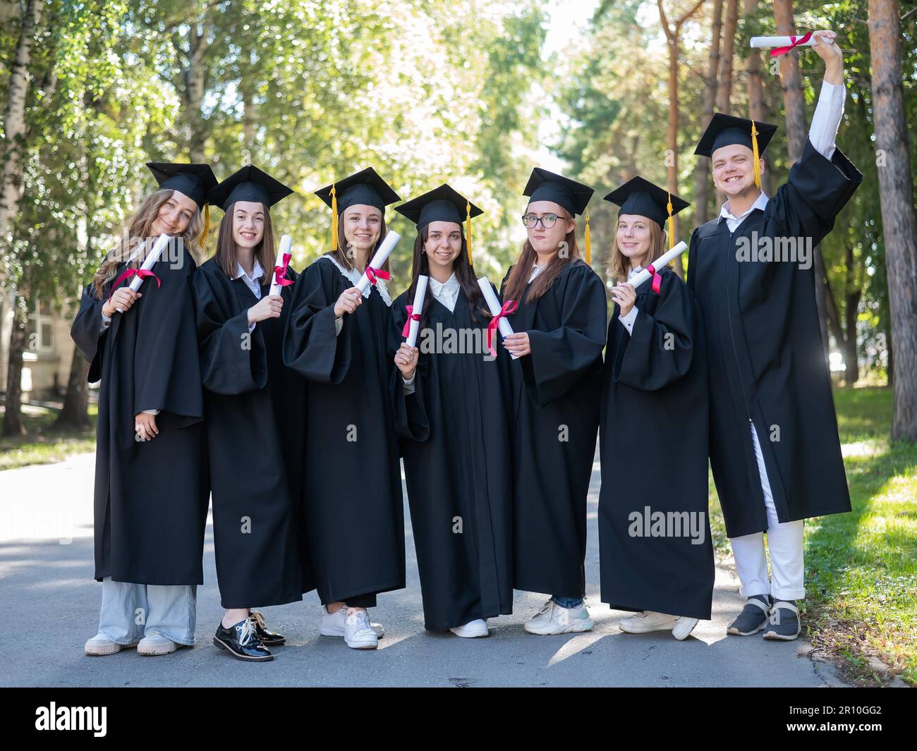 Row of young students in graduation gowns outdoors showing off their ...
