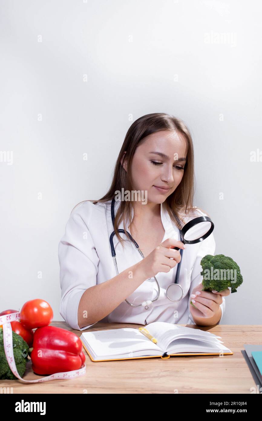 A female nutritionist looks through a magnifying glass at broccoli in ...