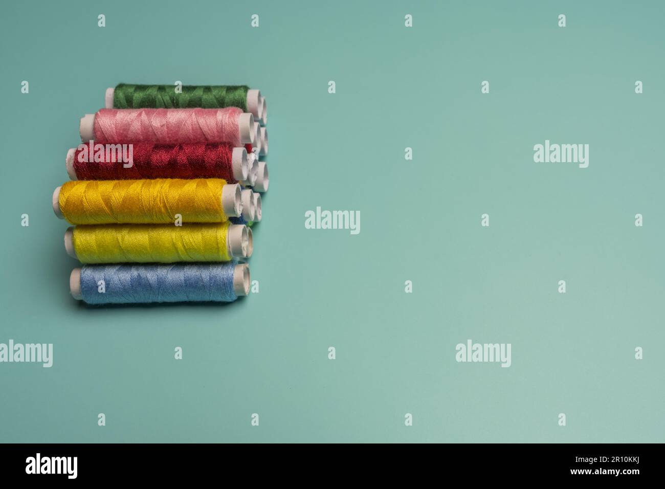 Spools of multi colored sewing thread stacked on a turquoise blue ...