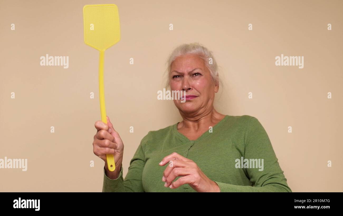 An elderly European woman is trying to catch a mosquito with a fly ...