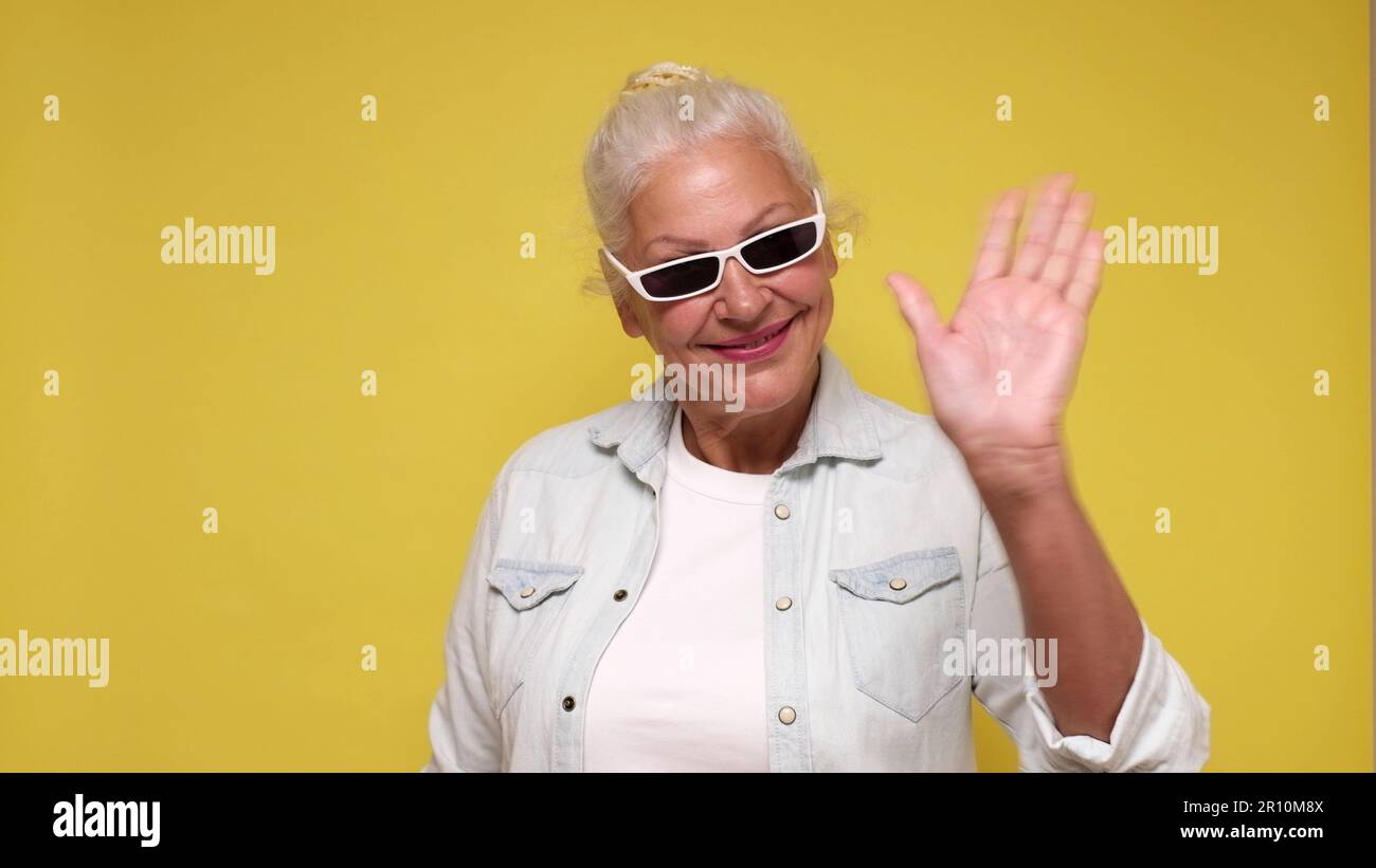 an elderly European woman greeting a friend, waving her hand and saying ...