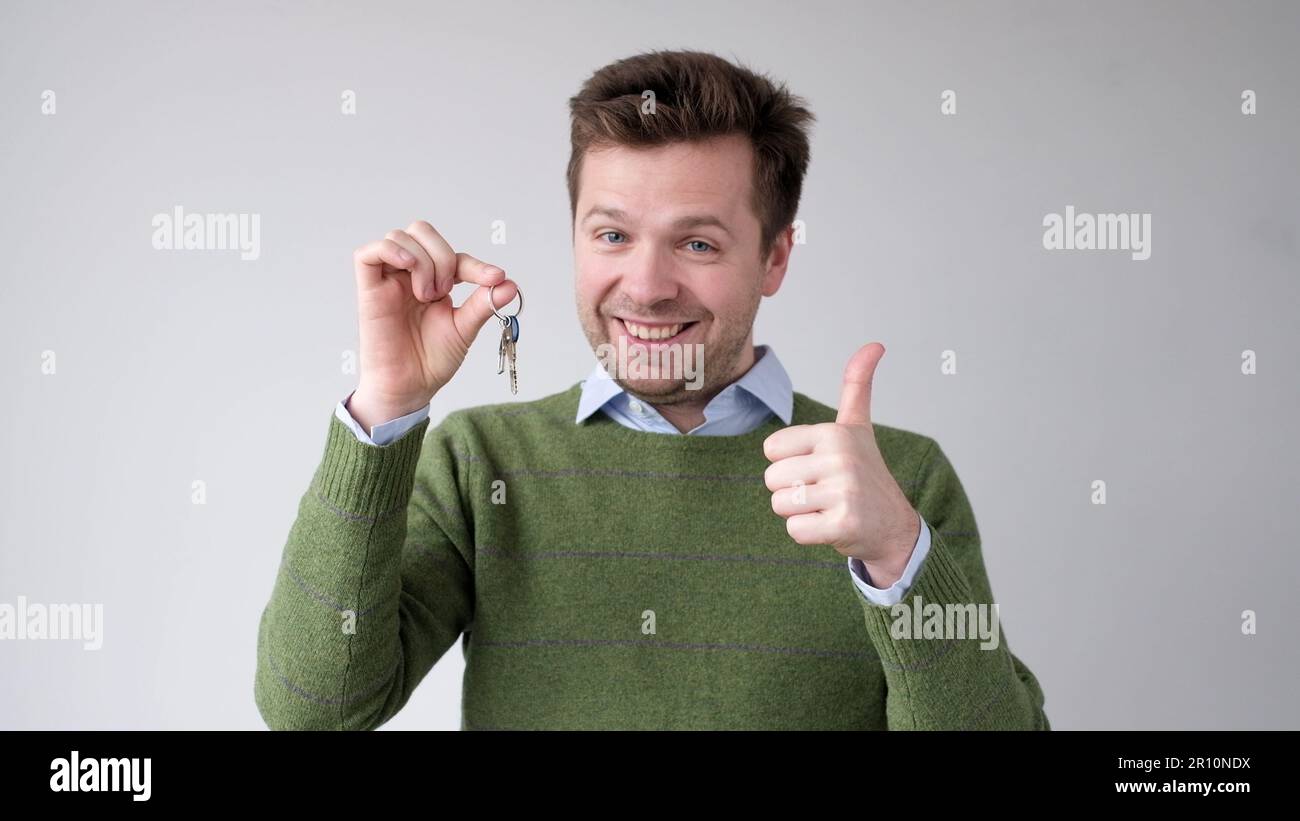A European young man shows the keys to his new apartment. He is happy ...