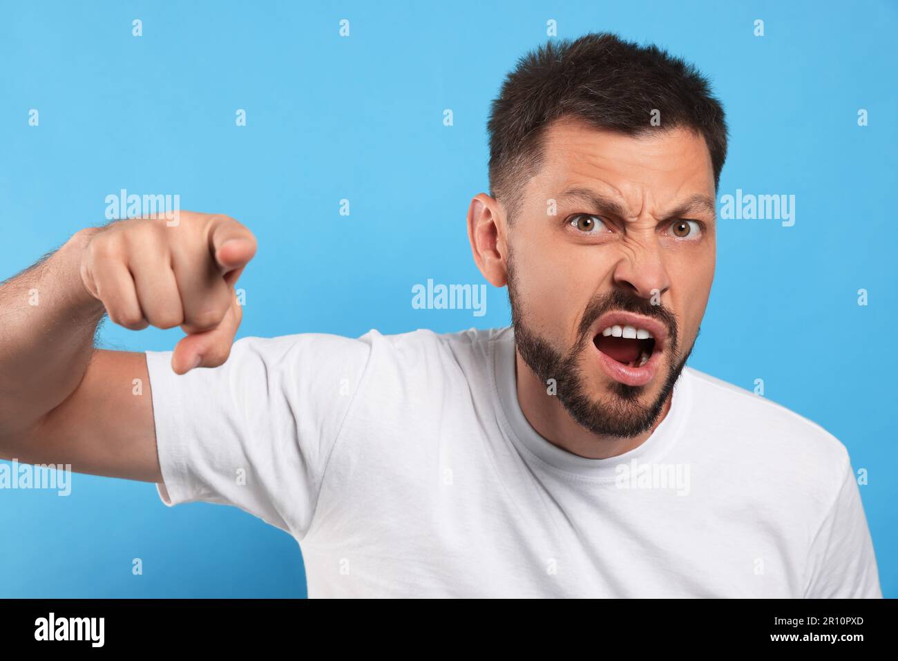 Aggressive man pointing on light blue background Stock Photo - Alamy