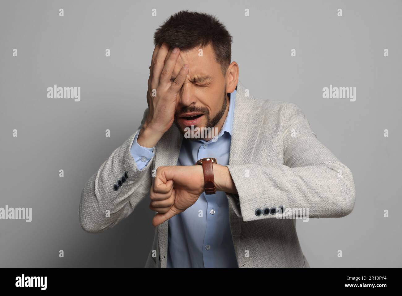 Emotional man checking time on grey background. Being late concept ...