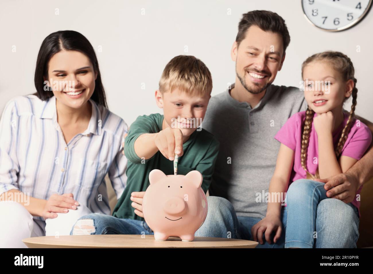 Happy family putting money into piggy bank at table in room Stock Photo ...