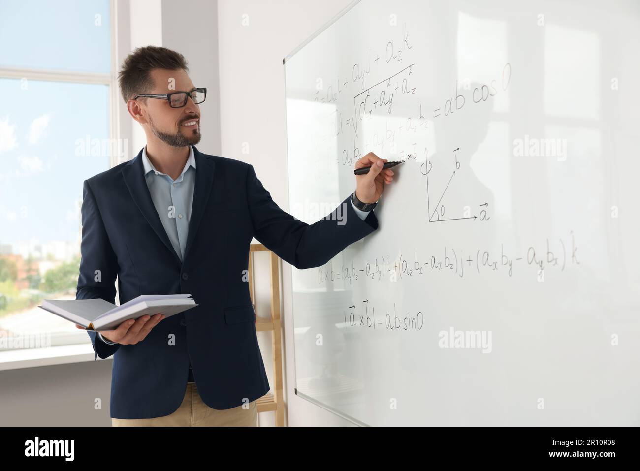 Happy teacher with book explaining mathematics at whiteboard in ...