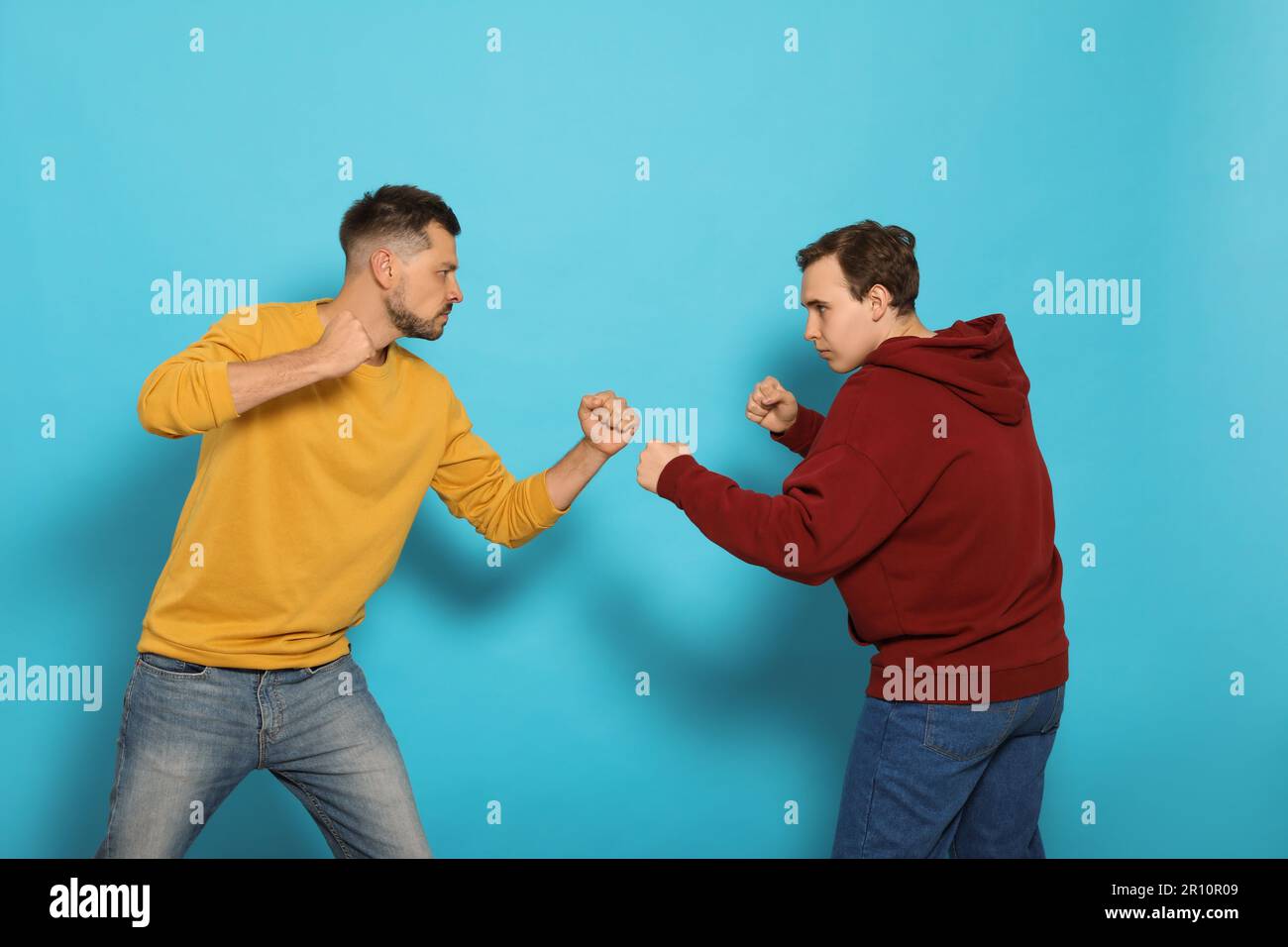 Two emotional men fighting on light blue background Stock Photo - Alamy