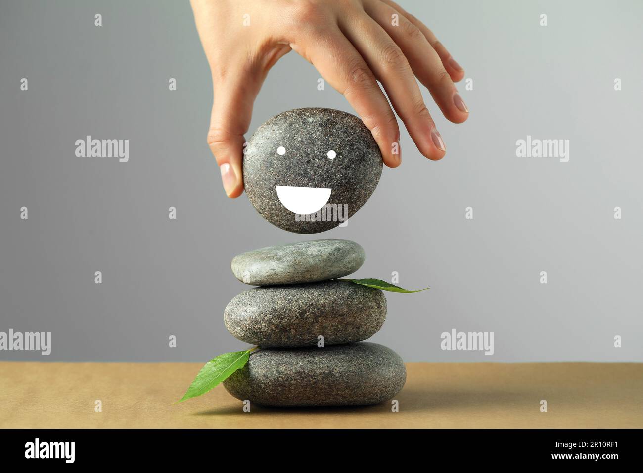 Woman putting stone drawn happy face onto stack against grey background ...