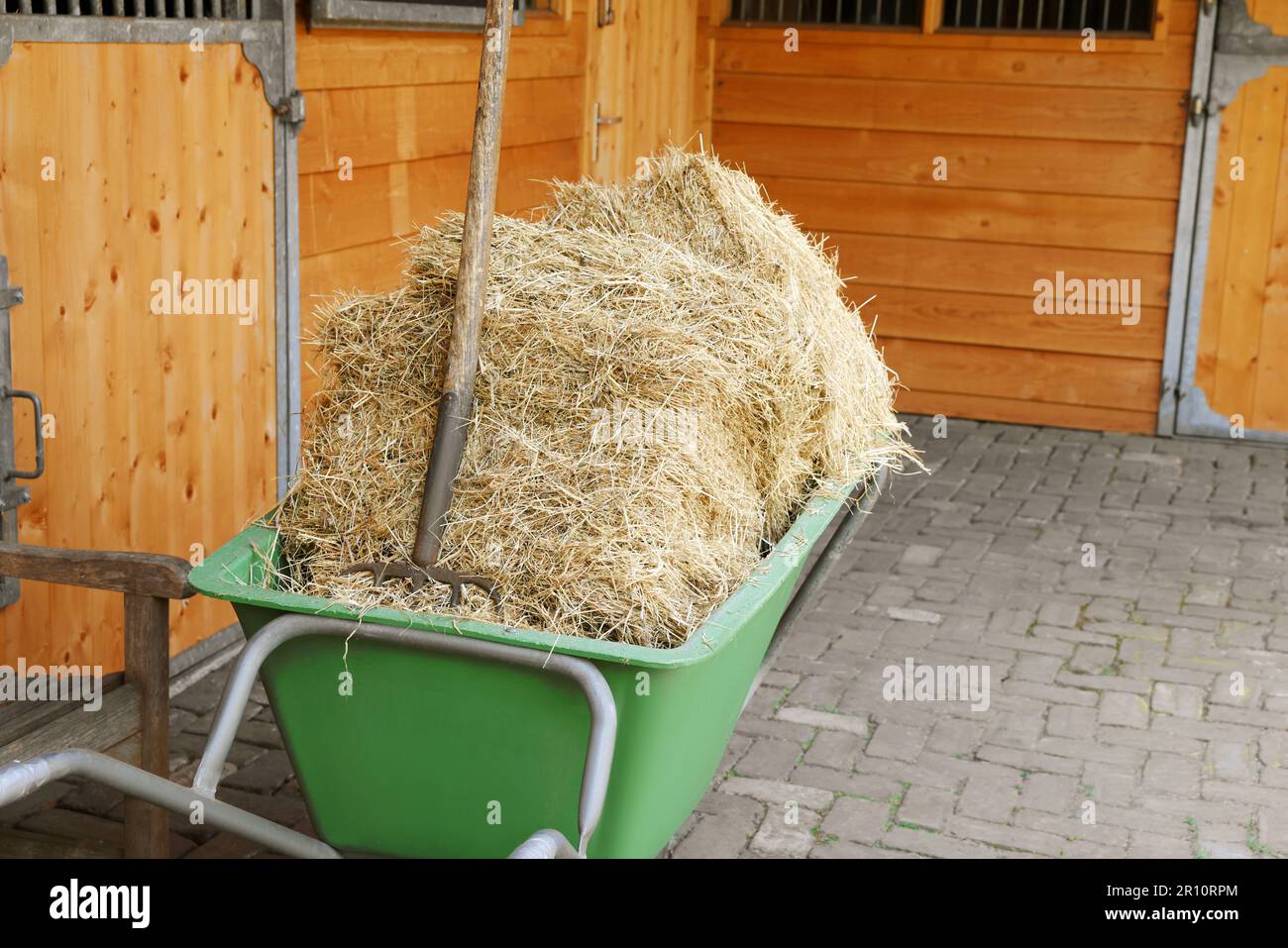 Wheelbarrow with hay near wooden stable outdoors Stock Photo - Alamy