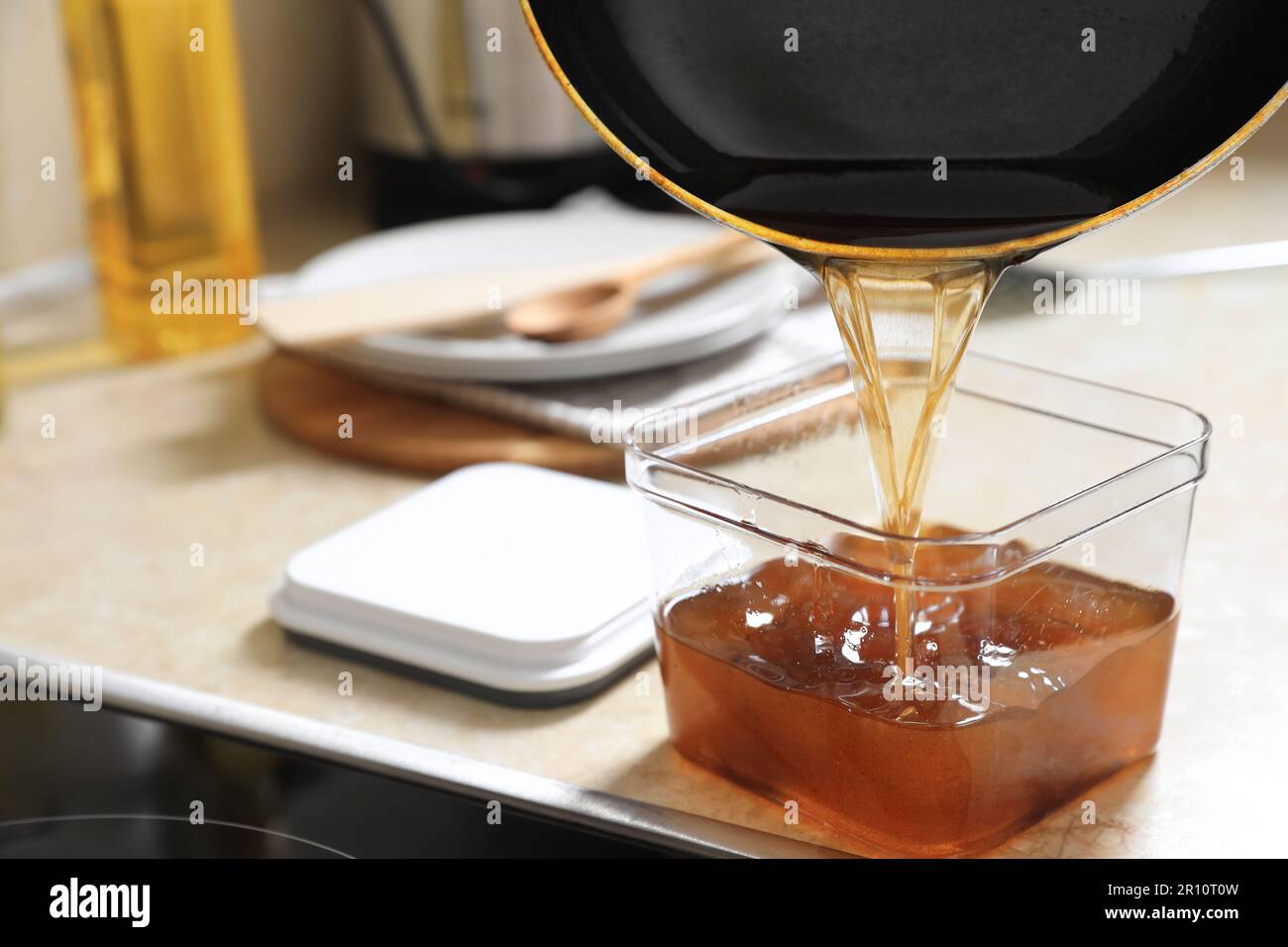 Pouring used cooking oil from frying pan into container on beige table ...