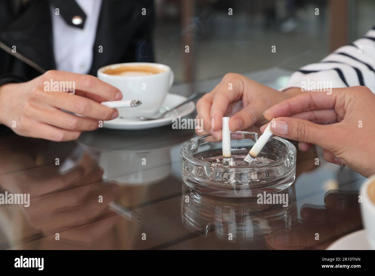 Women putting out cigarettes in ashtray at table, closeup Stock Photo ...