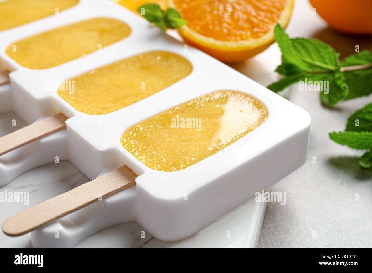 Tasty orange ice pops in mold on light grey table, closeup. Fruit ...
