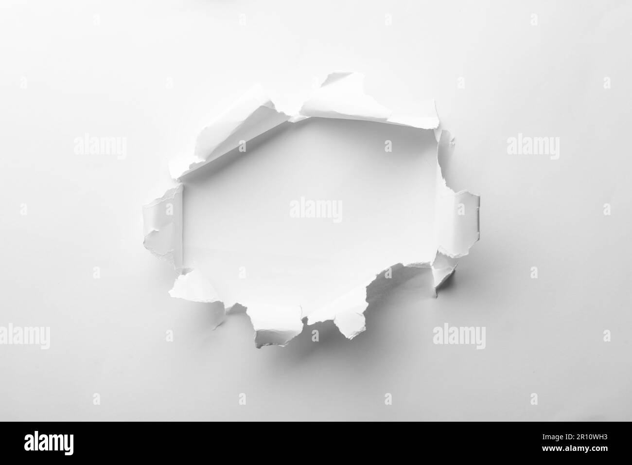 Hole in white paper on light background Stock Photo - Alamy