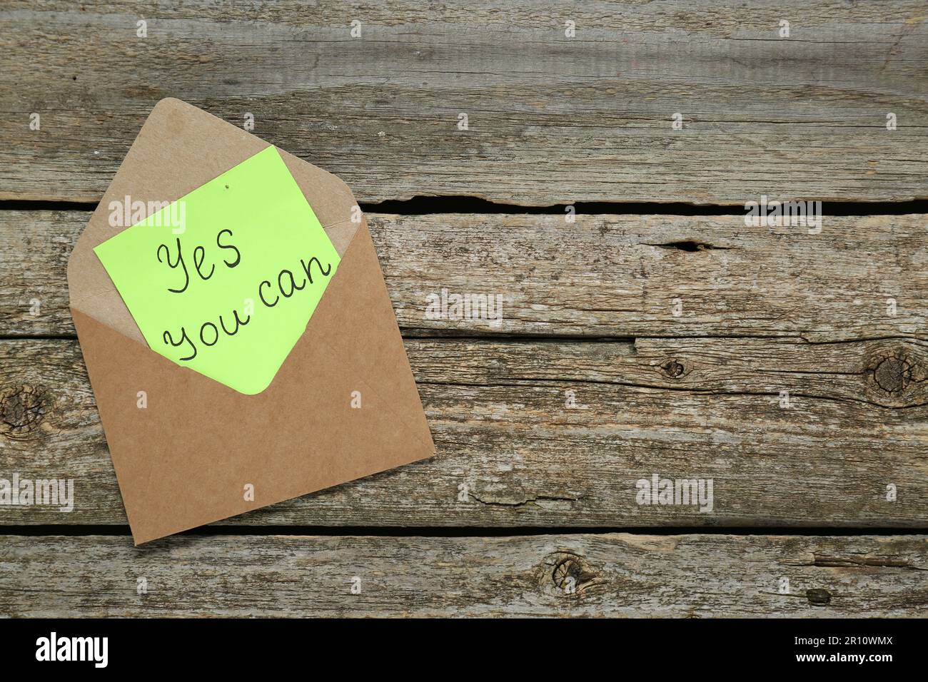 Envelope and phrase Yes You Can on wooden table, top view with space ...