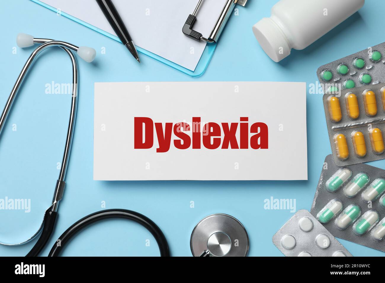 Card with word Dyslexia, stethoscope, pills and clipboard on light blue ...