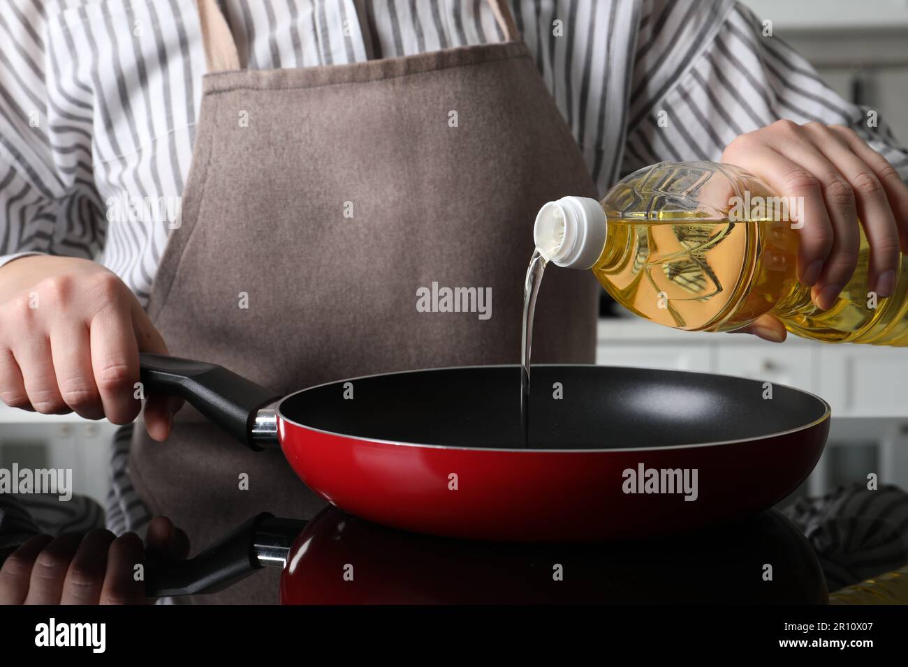 Woman pouring cooking oil from bottle into frying pan on stove, closeup ...