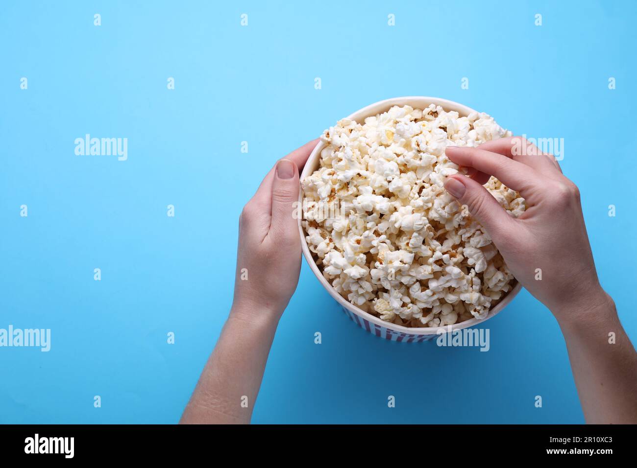Woman taking delicious popcorn from paper bucket on light blue ...