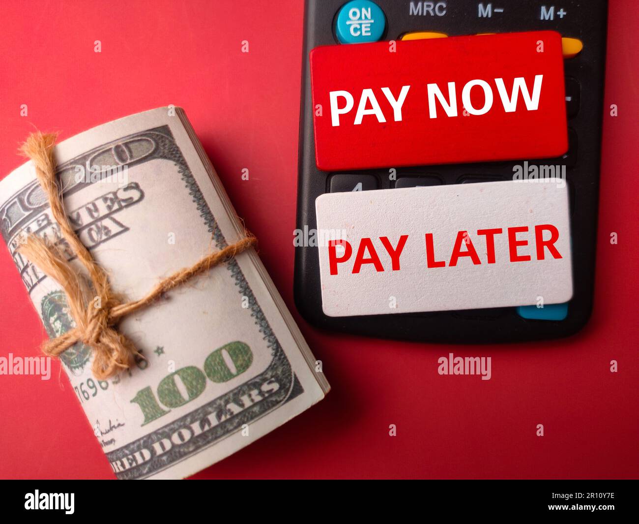 Banknotes and calculator with word PAY NOW PAY LATER on a red ...