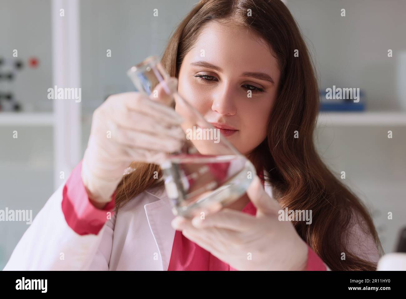 Smiling woman scientist holding flask with transparent liquid in hands ...