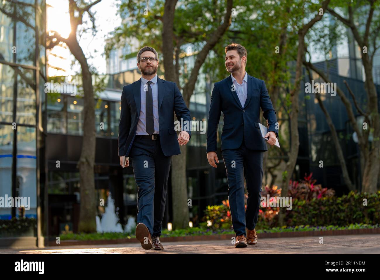 Photo of businessmen in suits walking outdoor through city street. Two ...