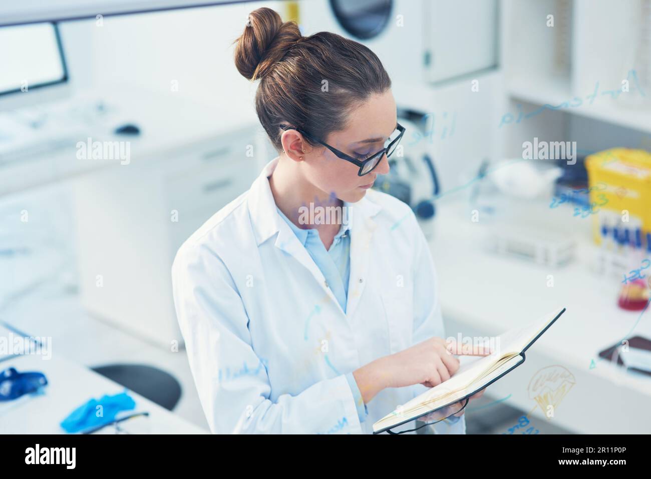Thank goodness I made a note. a focused young female scientist reading ...