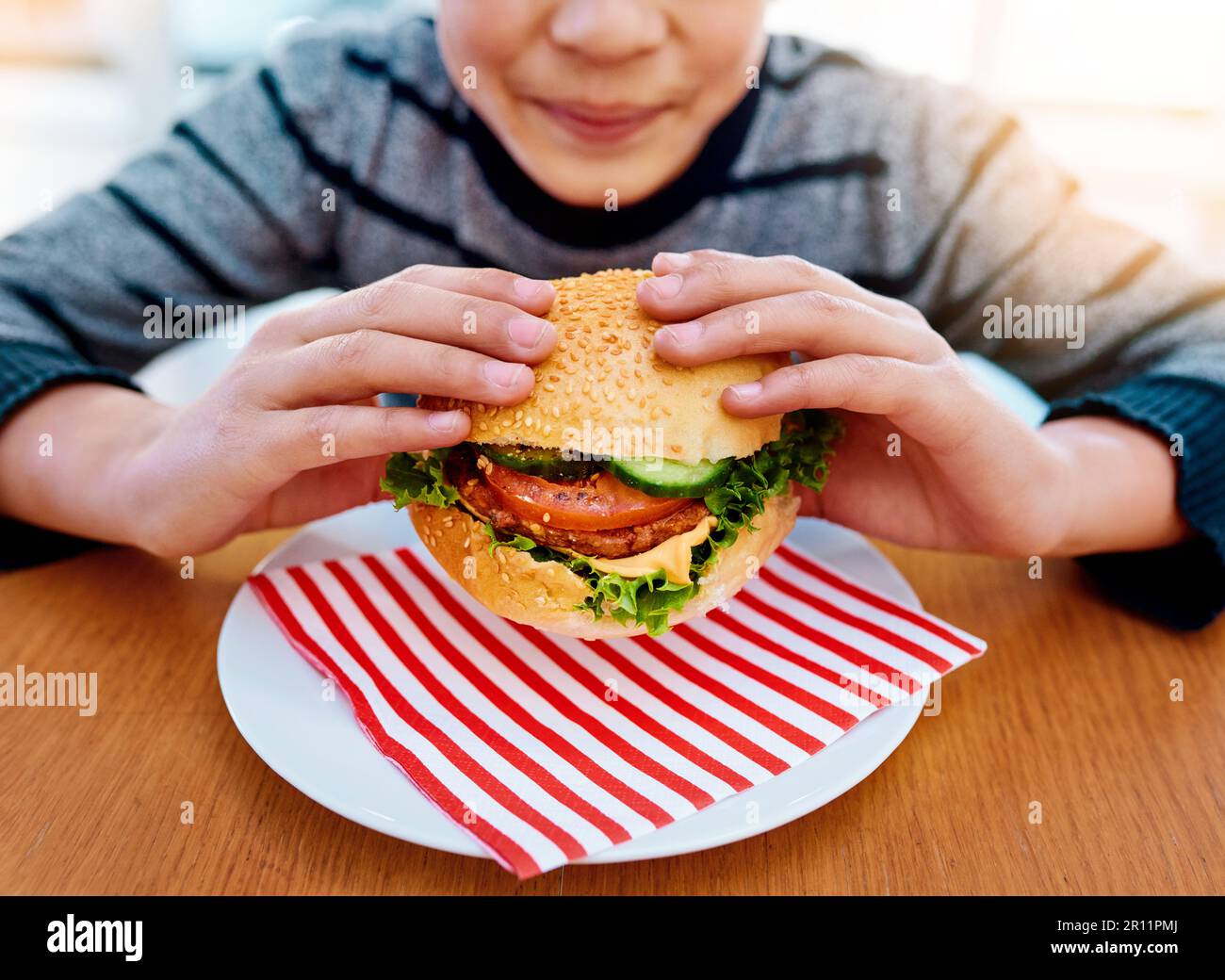 Child, hands and eating burger on table for delicious lunch, meal or ...