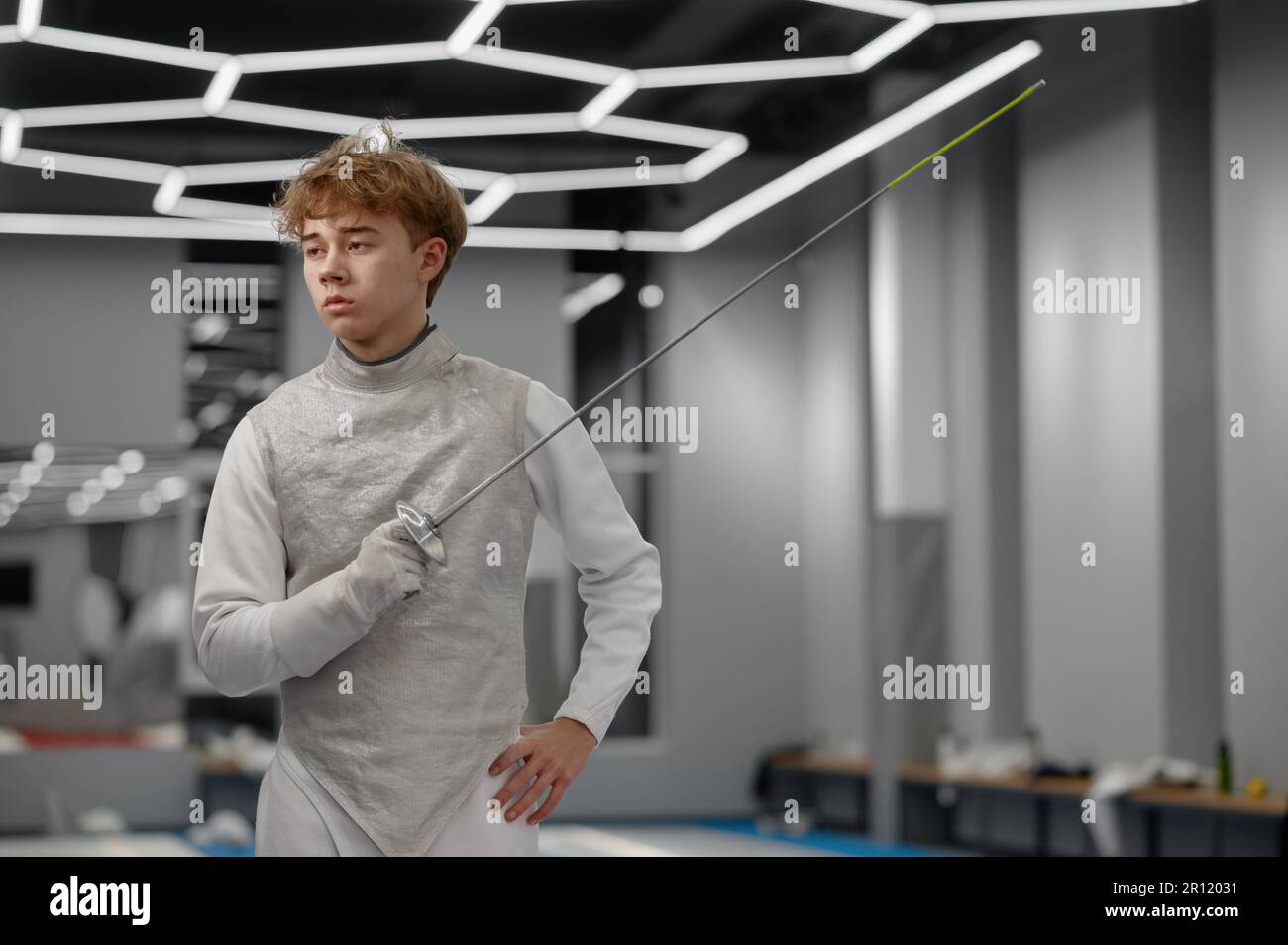 Portrait of teenager fencer wearing white fencing costume with sword ...