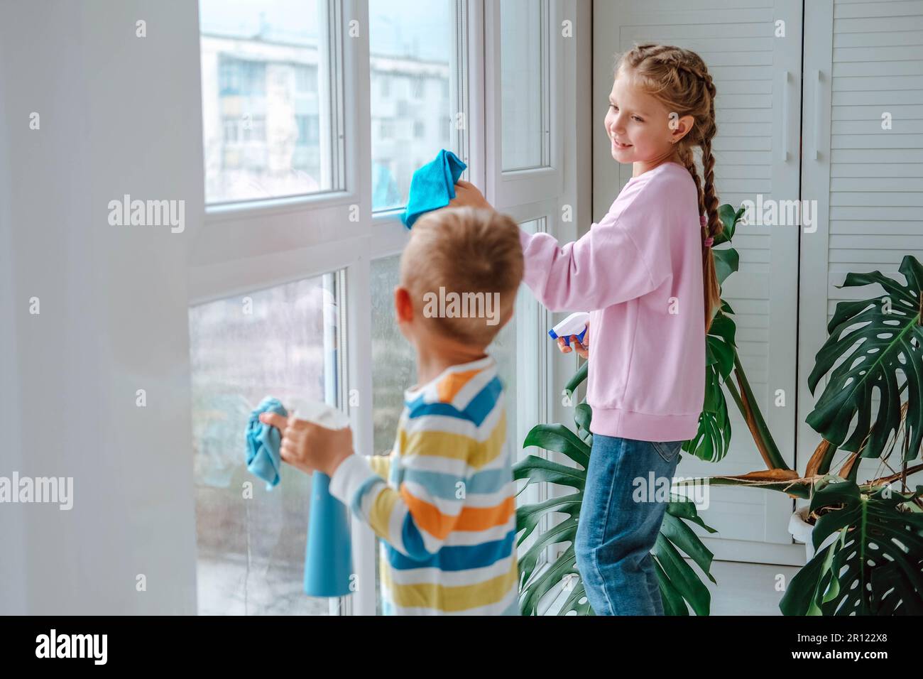 Little boy and girl sprinkles water from a bottle on the window and ...