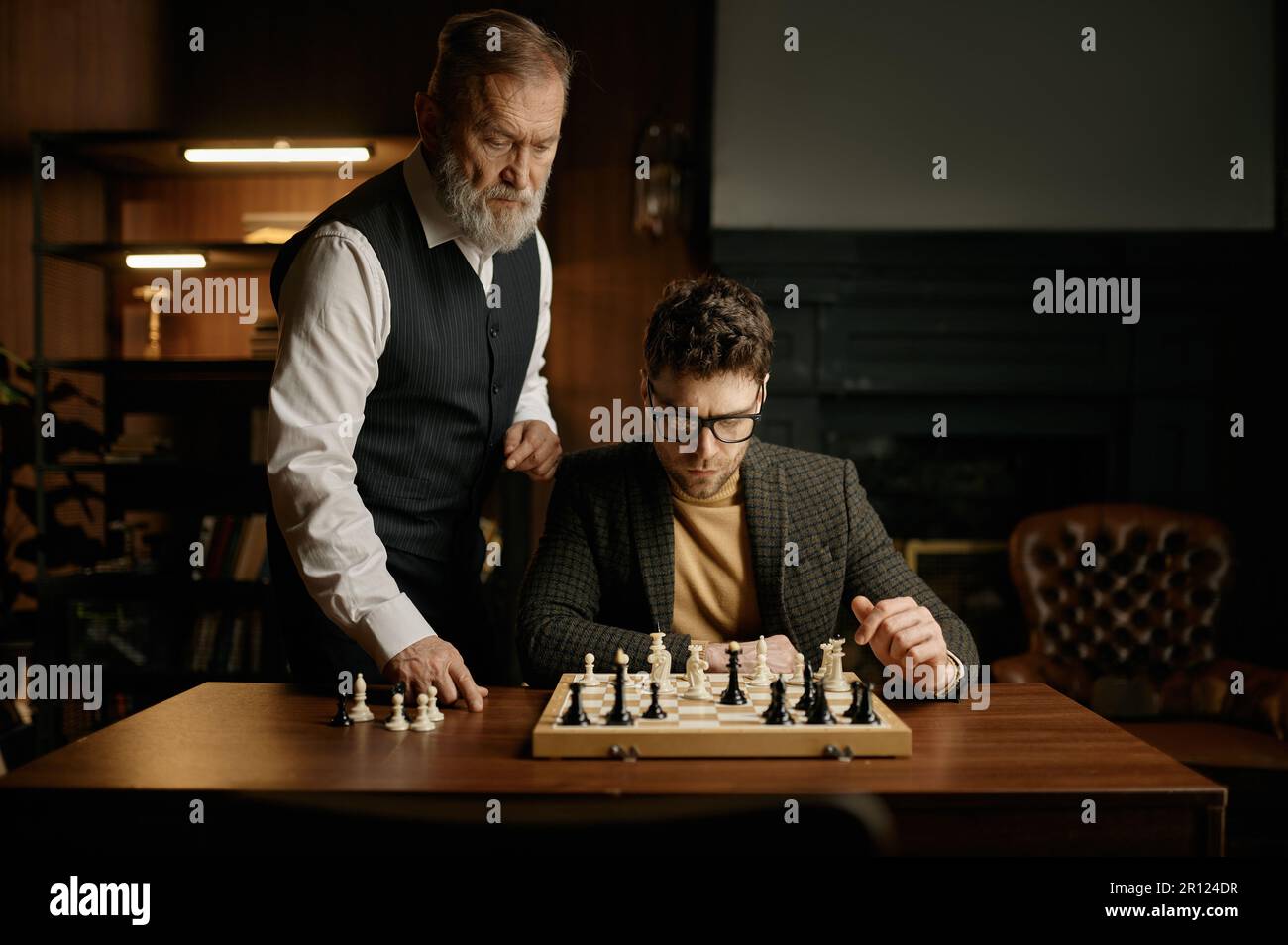 Senior man teaching young guy playing chess explaining rules of game ...