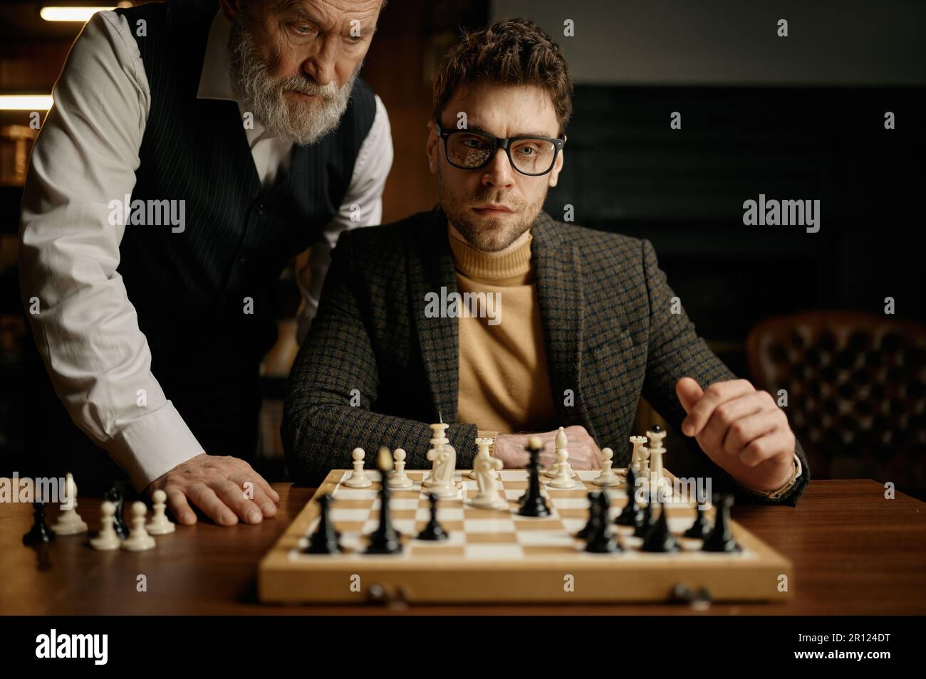 Senior man teaching young guy playing chess explaining rules of game ...