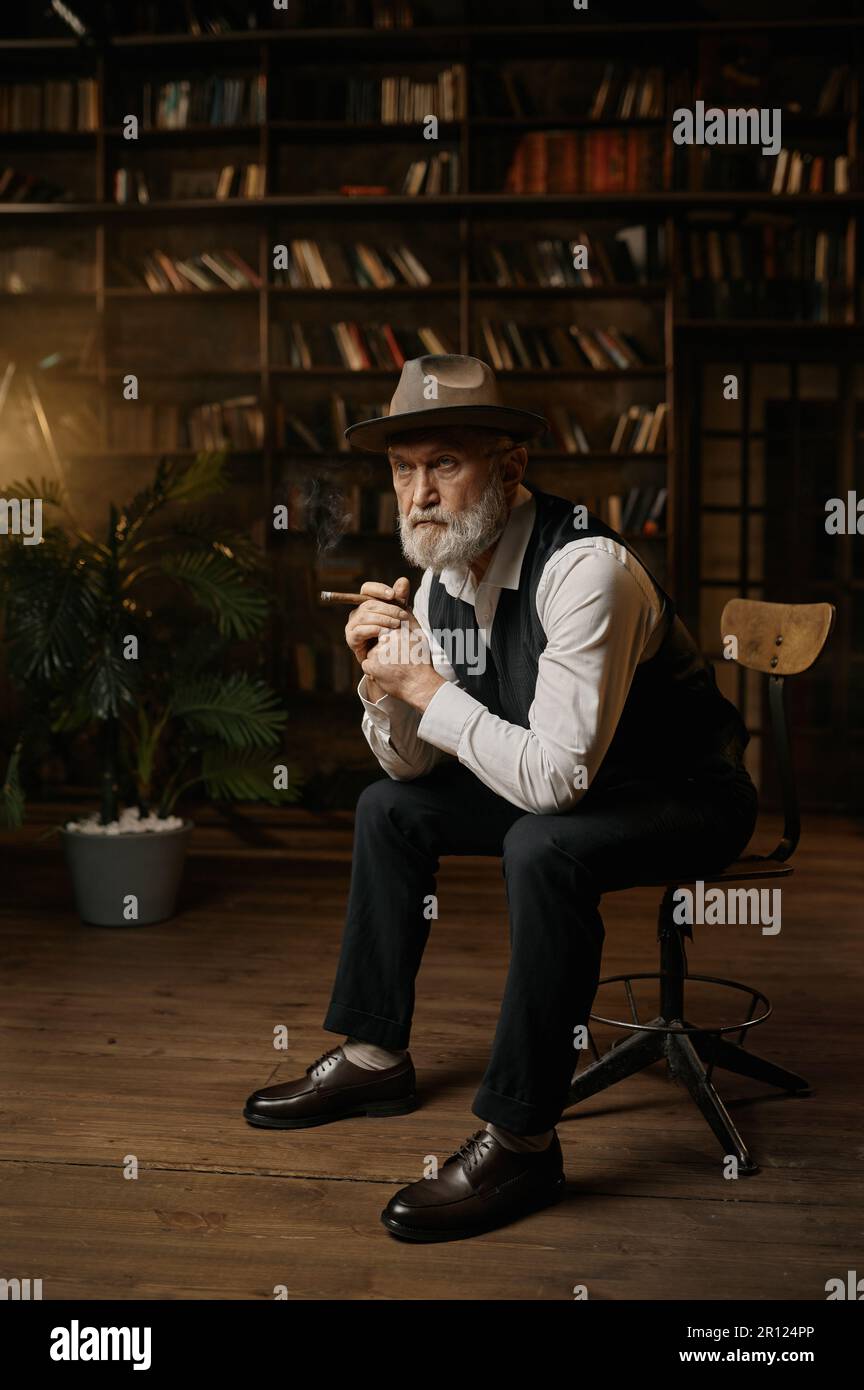 Elegant elderly business man sitting on vintage chair smoking cigar Stock Photo - Alamy