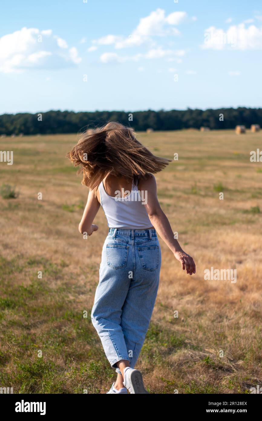 A young woman walking in an open field, her long, dark hair blowing in ...
