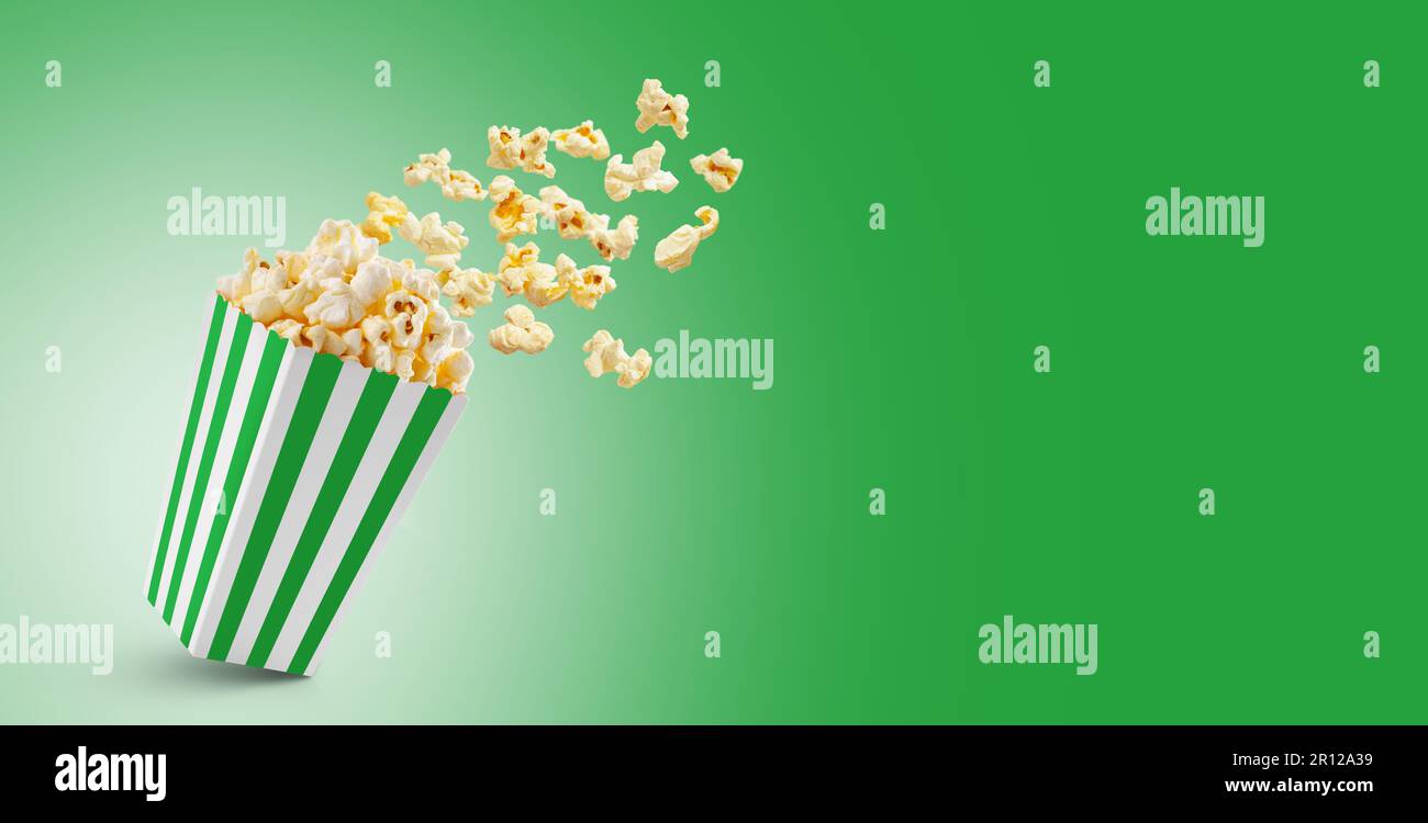 Popcorn flying out of green white striped paper box isolated on green ...