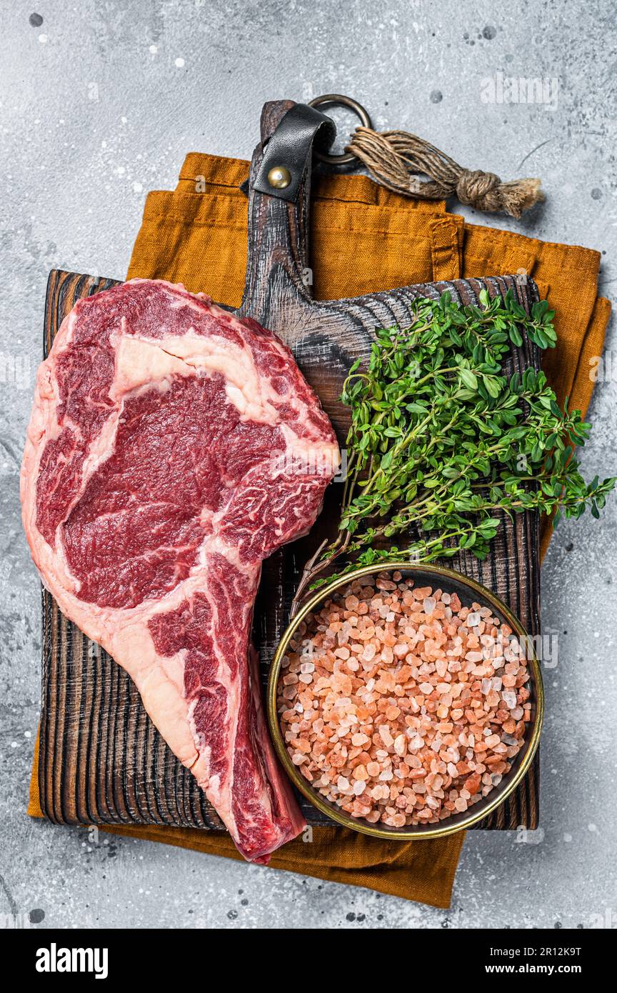 Raw uncooked black angus beef cowboy or rib eye steak. Gray background ...