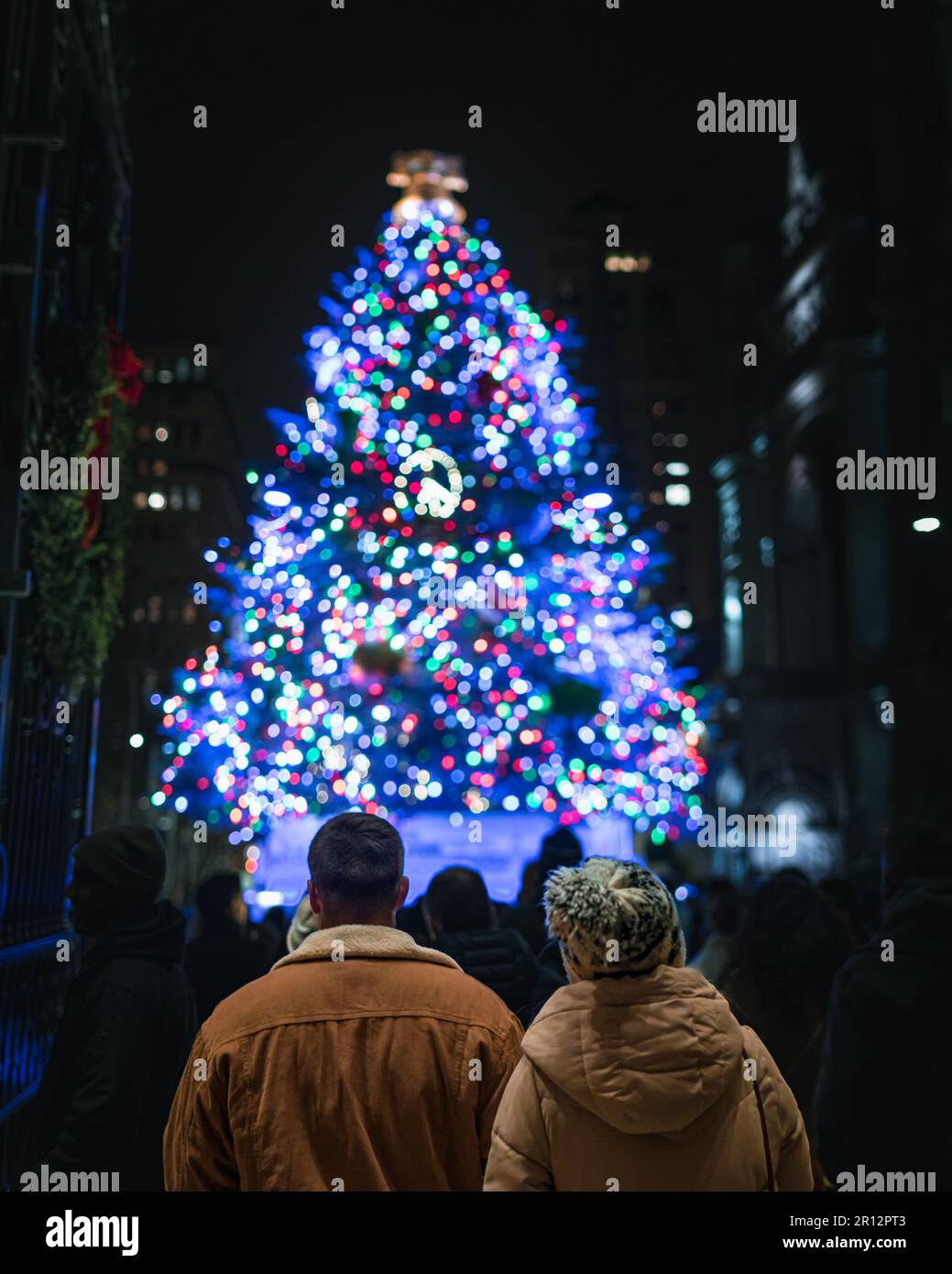 A group of people admiring a vibrant Christmas tree in the city ...