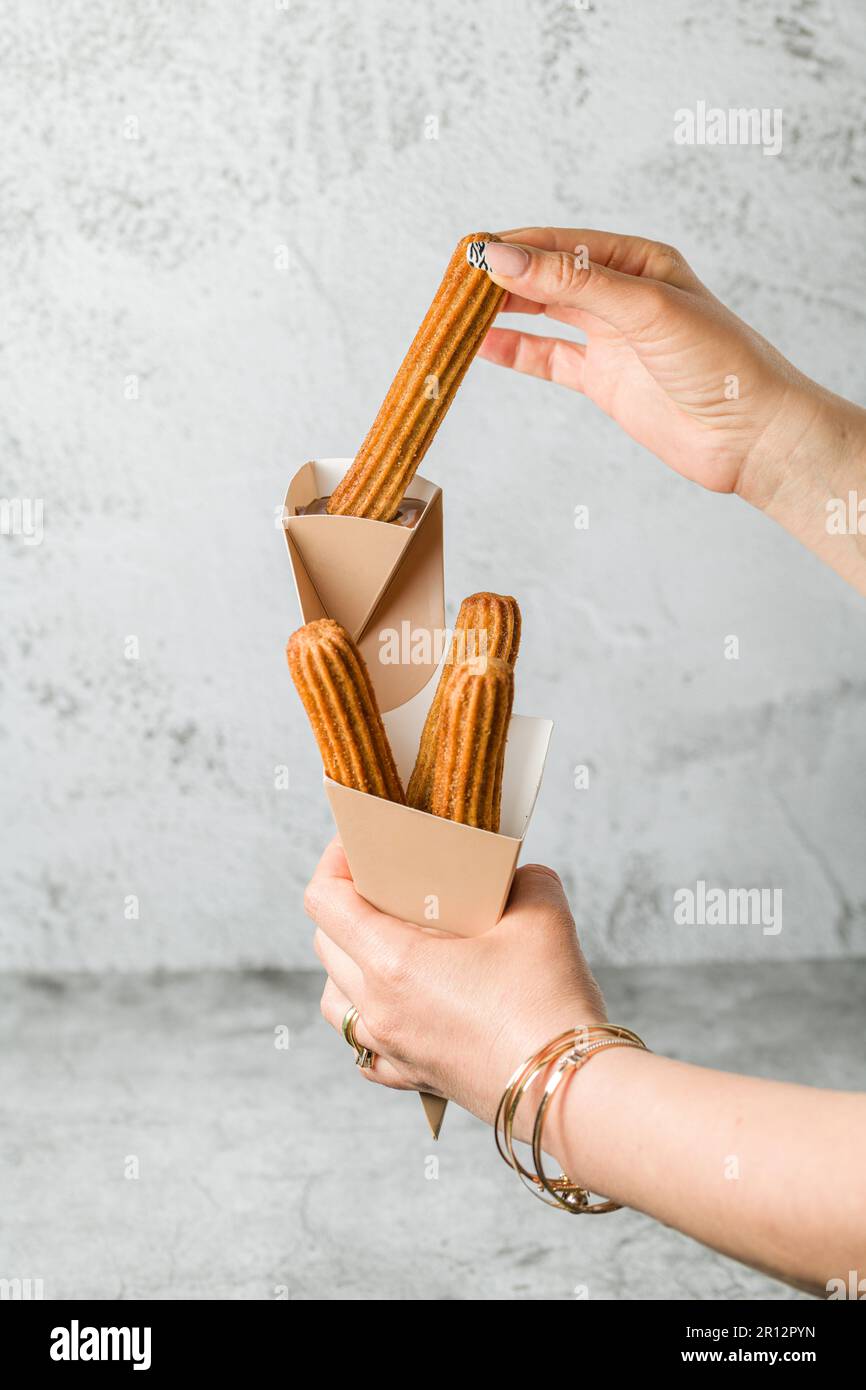 Woman taking churros from a cone and dipping it in chocolate sauce ...