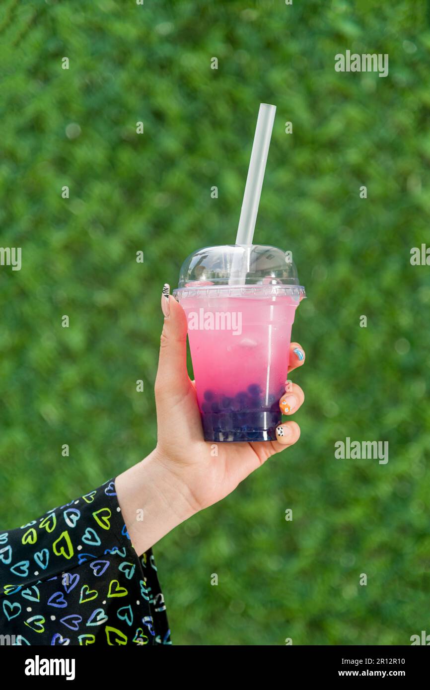 Woman holding bubble tea with lemonade in front of green grass wall ...