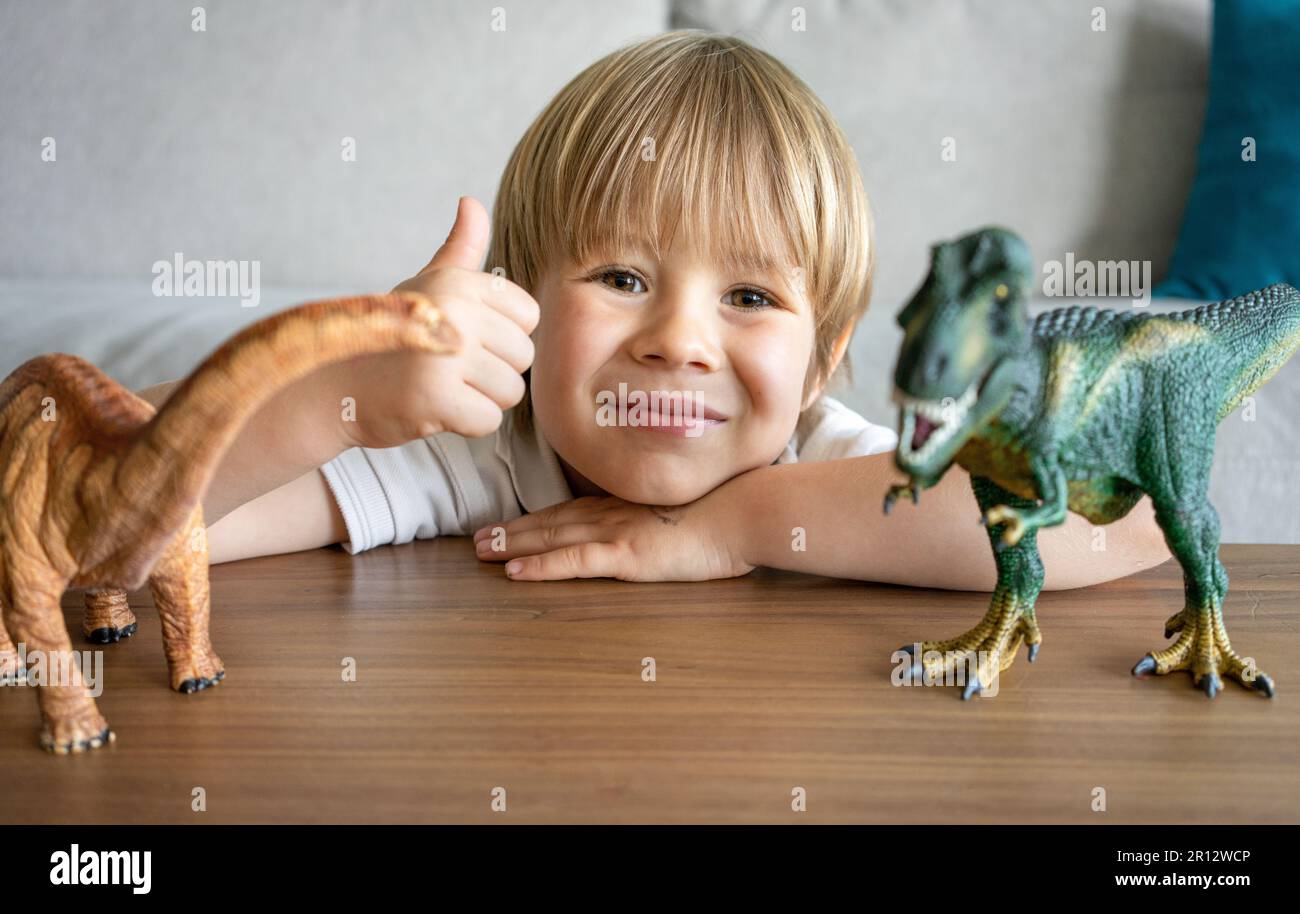 Little smiling boy playing with dinosaurs showing thumb up at home ...