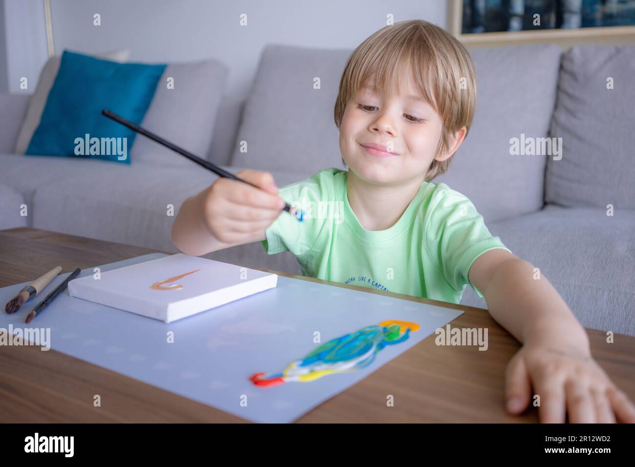 Young boy painting decorative green lettering on a sketchpad with a ...