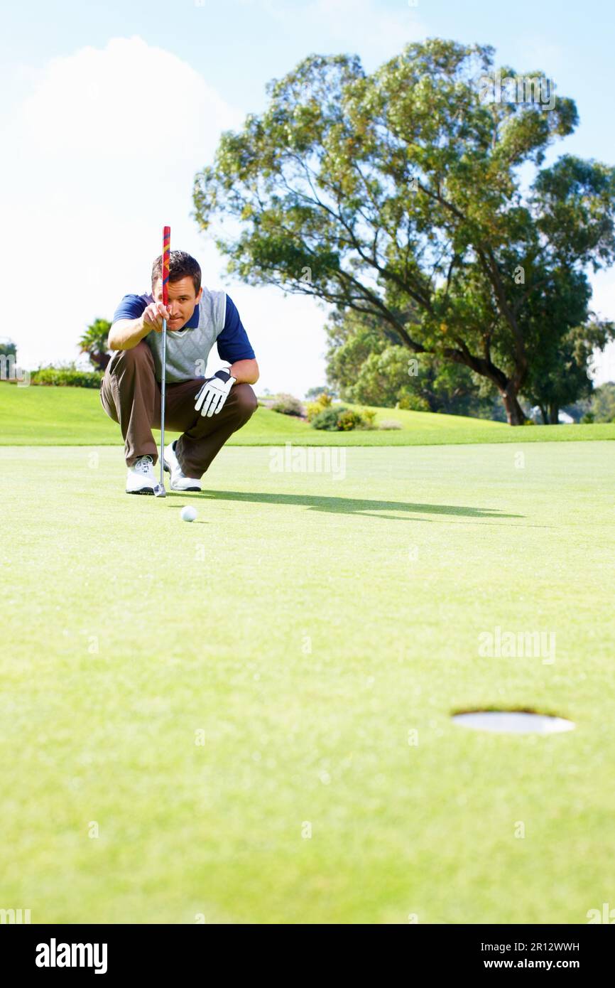 Male golfer lining up the putt. Full length of crouched male golfer on the putting green lining ...