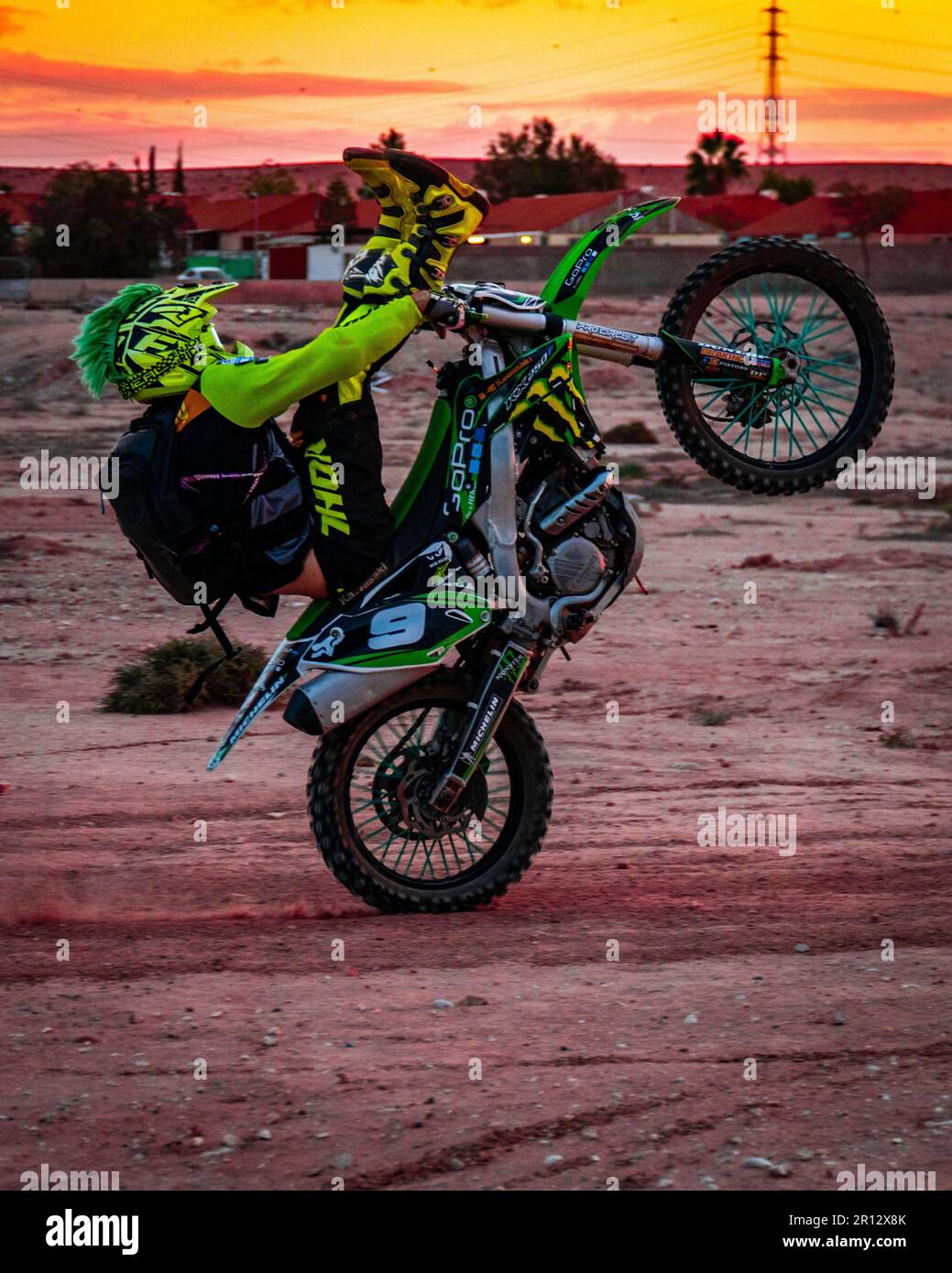 A man performing an aerial motorcycle stunt mid-air against a sunset ...