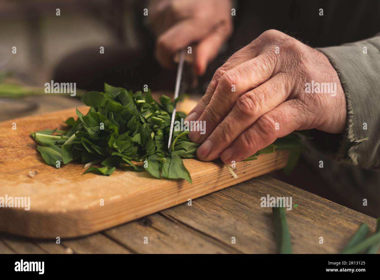 Human hands cutting wild garlic on wooden board for salad Stock Photo ...