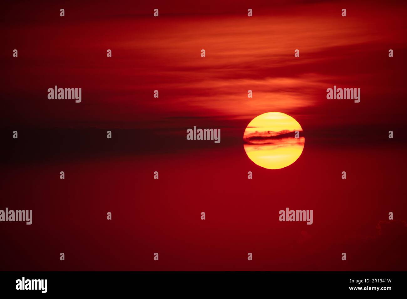 A vibrant setting sun seen in the distant blood red sky, emitting a ...