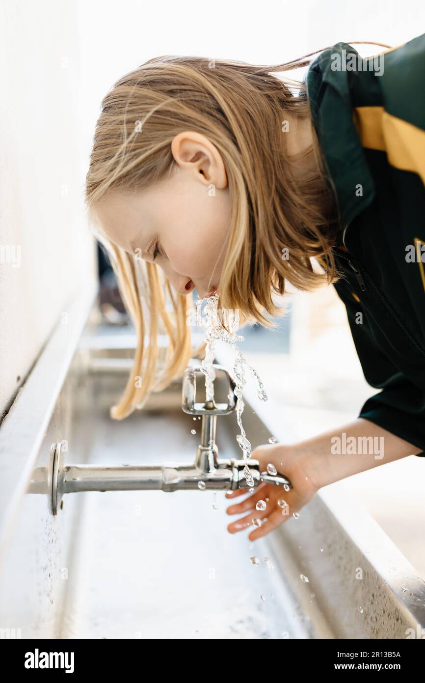 An Australian primary school girl drinking out of a water tap bubbler in the school yard at ...