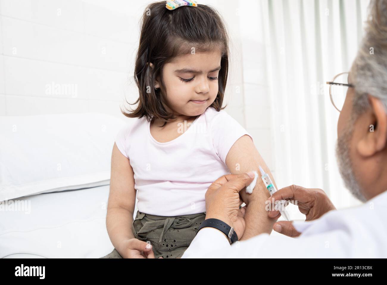Senior Indian man pediatrician performs a vaccination of a little girl ...
